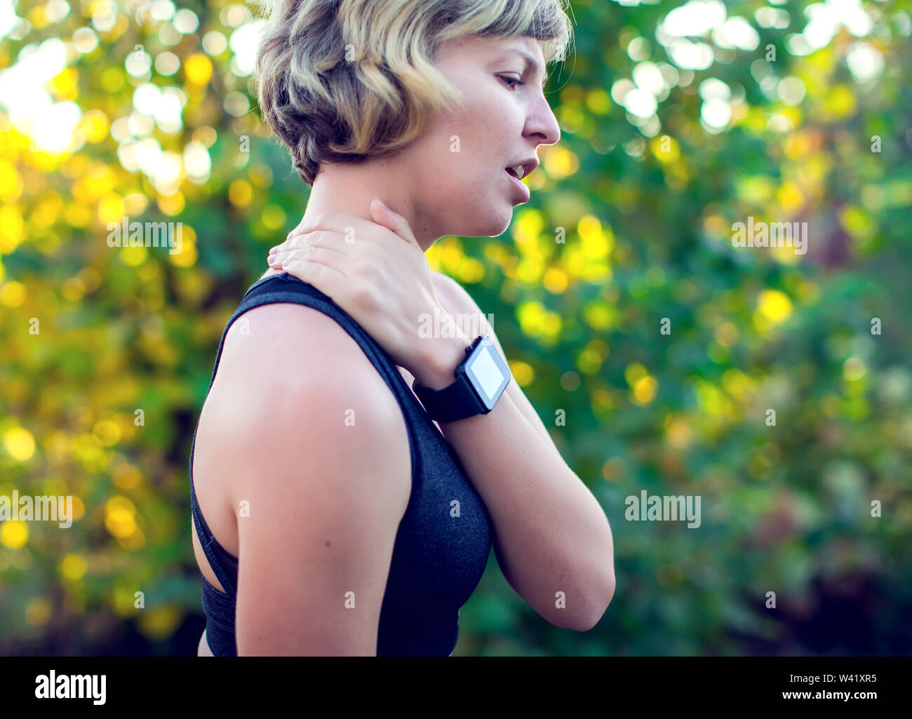 Woman in sportswear touching her neck by painful injury, over a nature ...