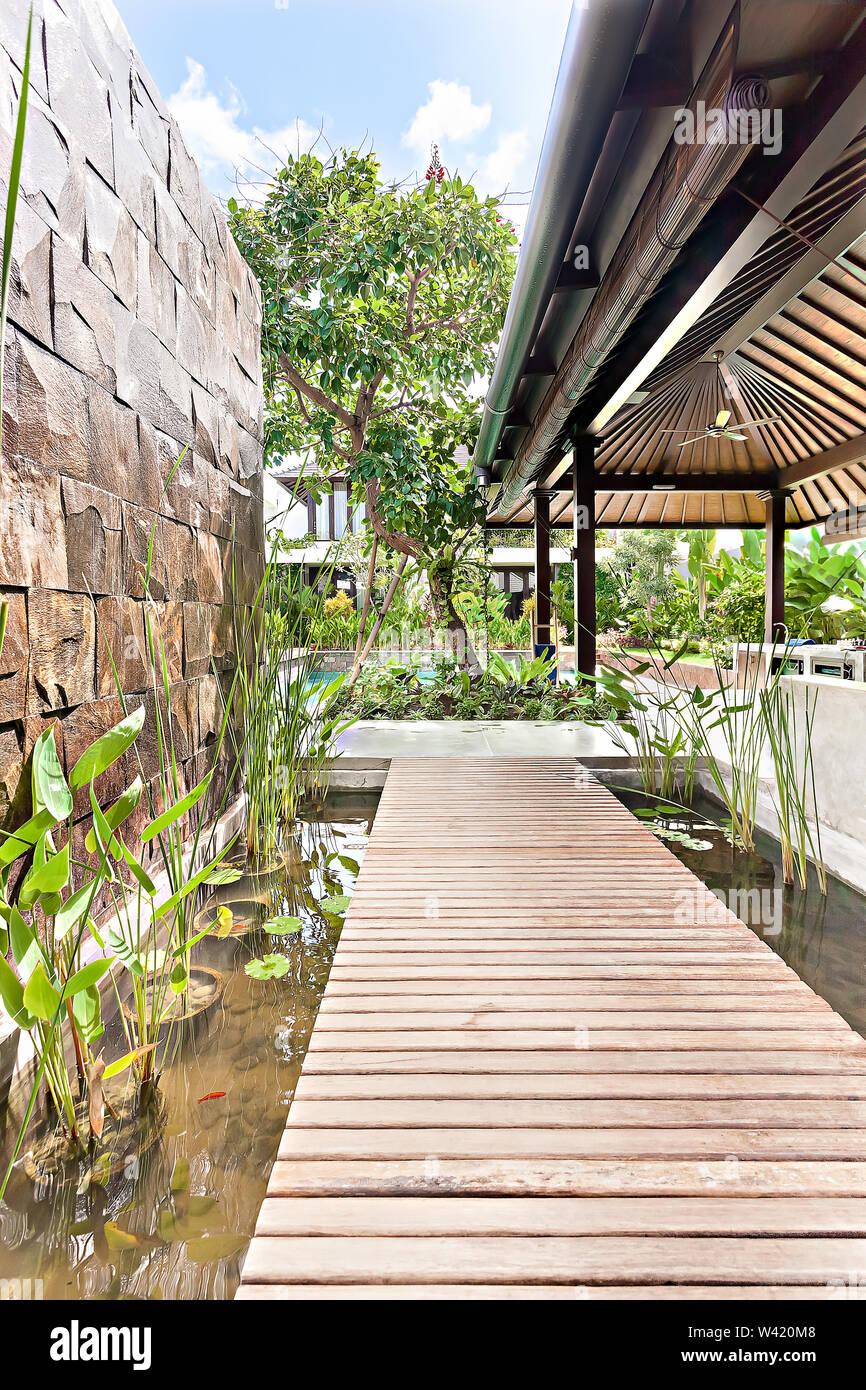 Wooden path over water pond in a modern hotel under traditional roof ...