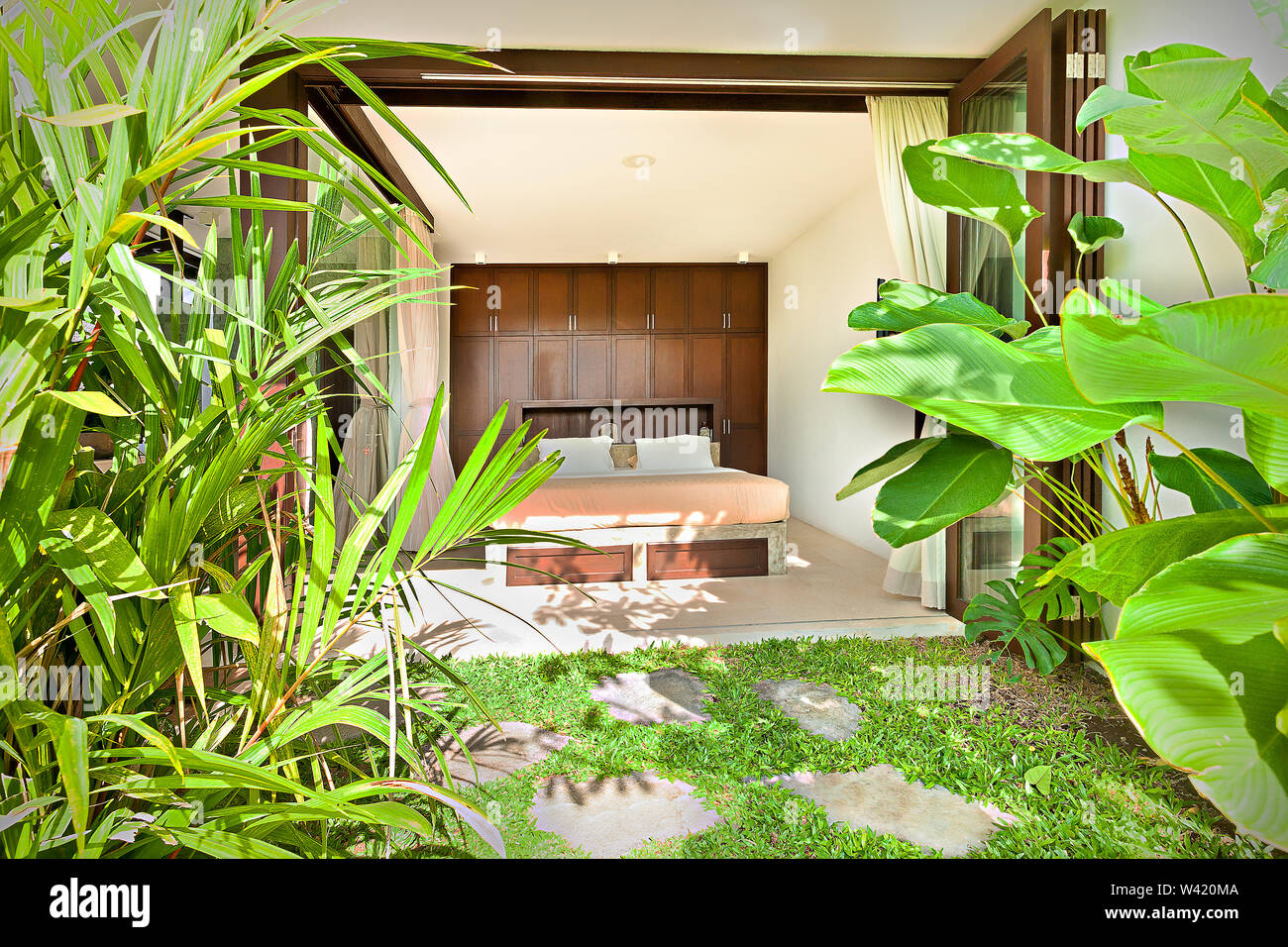 Outdoor bedroom in a luxury house with green plants, garden and a lawn ...