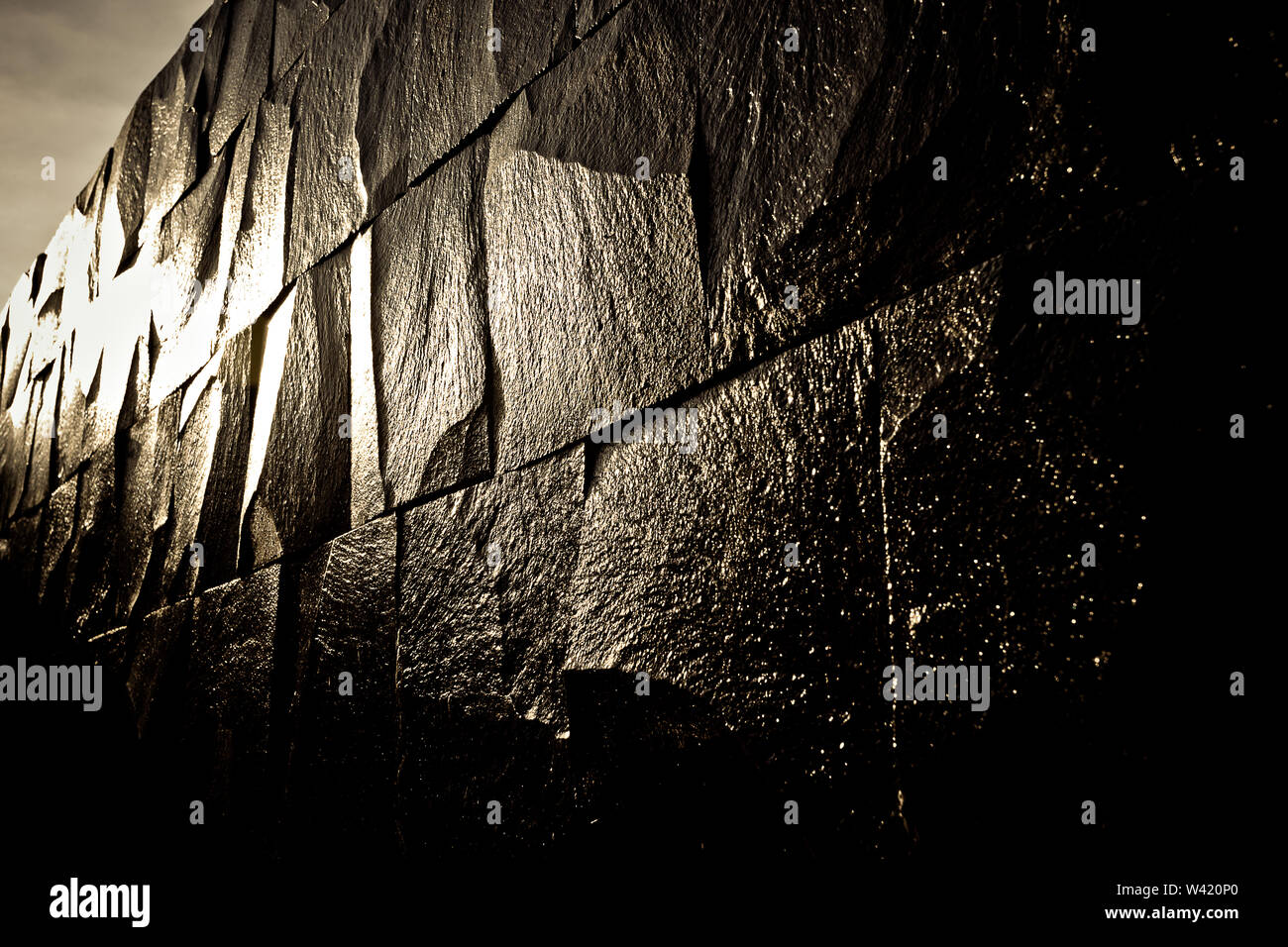 Dark stone wall shining with the light and giving the reflection wet ...
