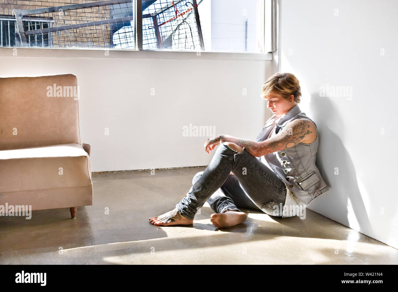 Young girl with a tattoo on her legs and arms sitting and bend over ...
