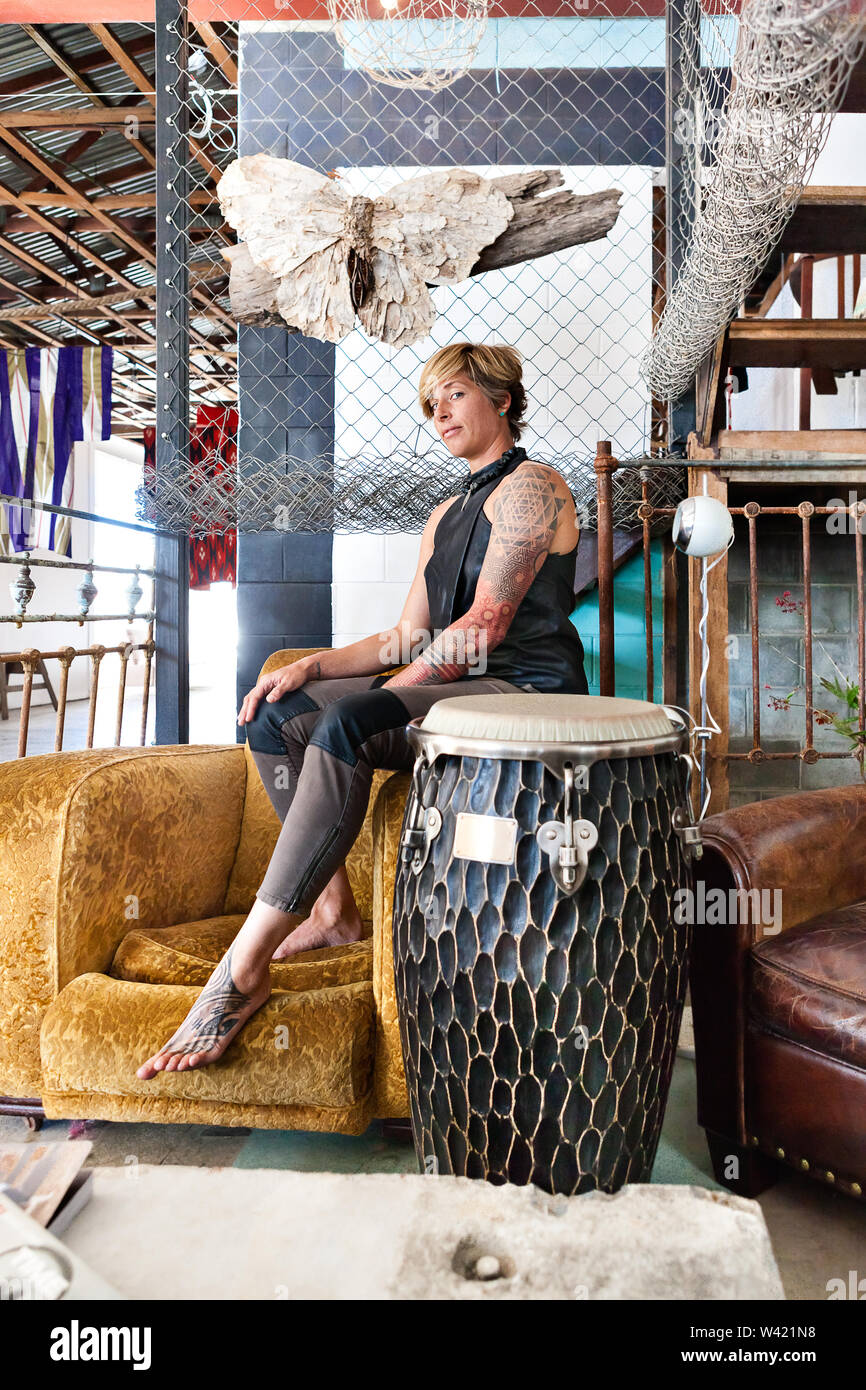 Teenage girl with a tattoo and a black dress sits on a yellow sofa and ...