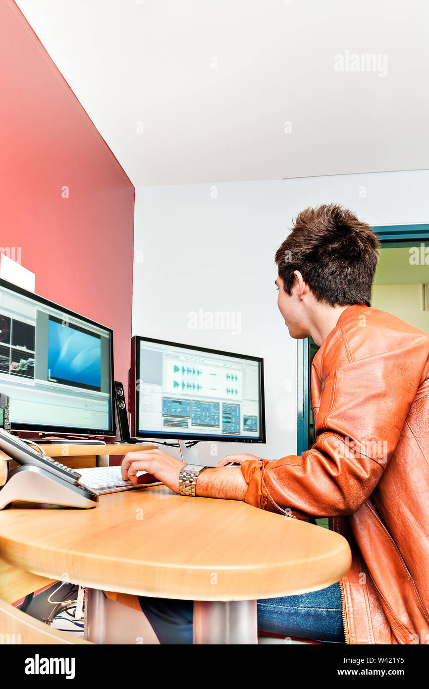 Young guy operating a computer with two screens in a private room and ...