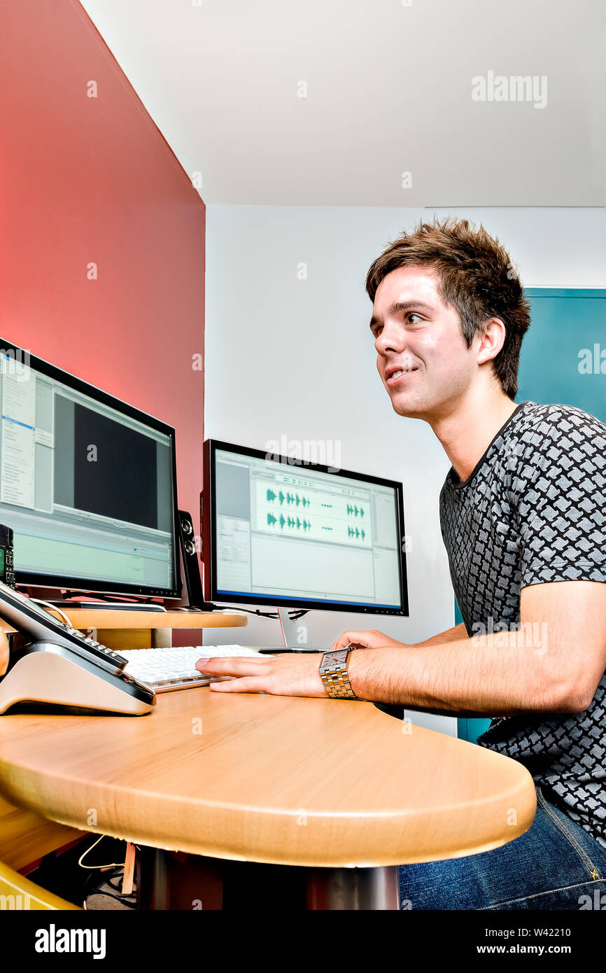 Young student laughing and operating a computer with more screens like ...