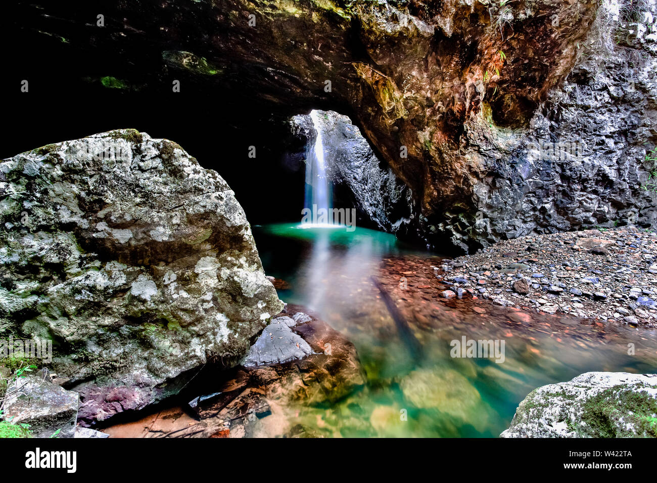 Inside the waterfall falling down of a stone cave that brighten with ...