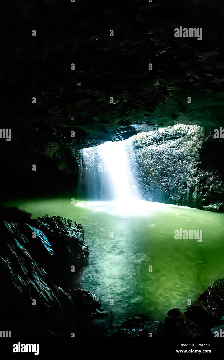 Shiny waterfall flows in the dark stone cave that brighten with the ...