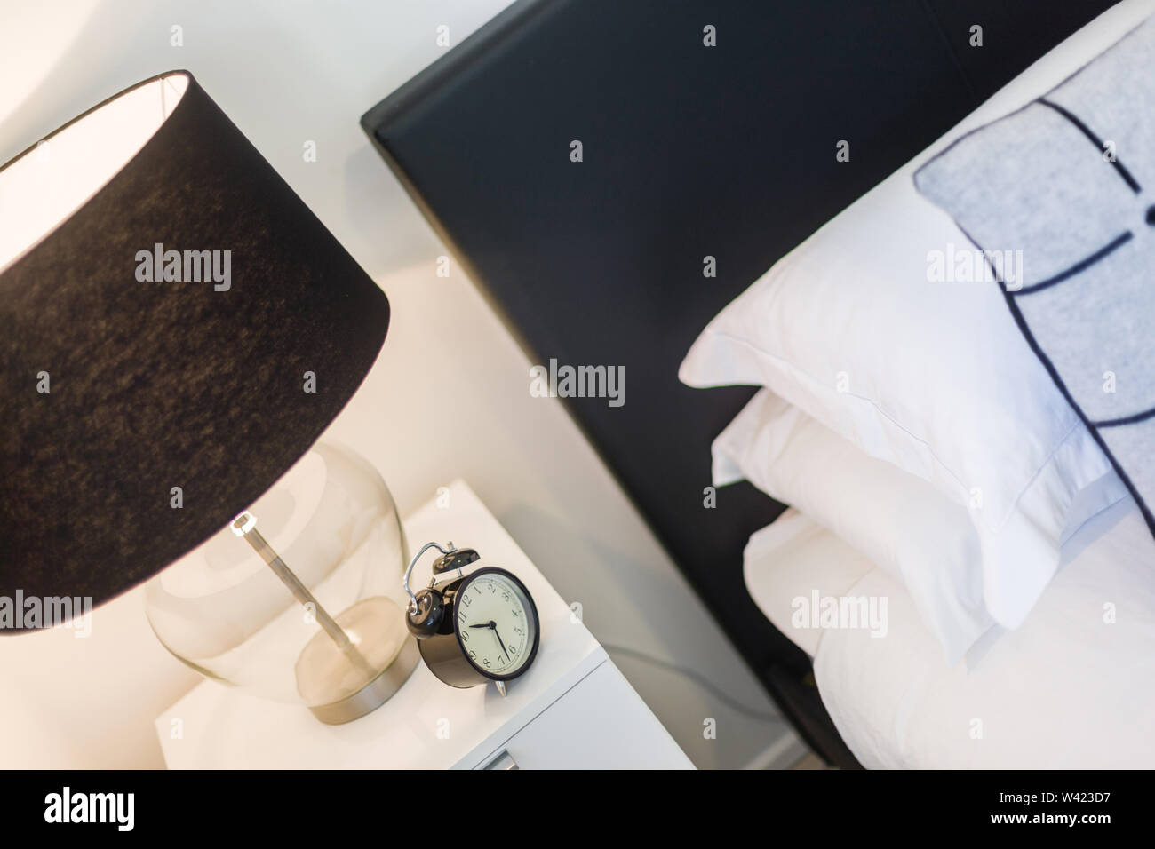 A tilted view of a lamp shade and alarm clock kept on a side table ...