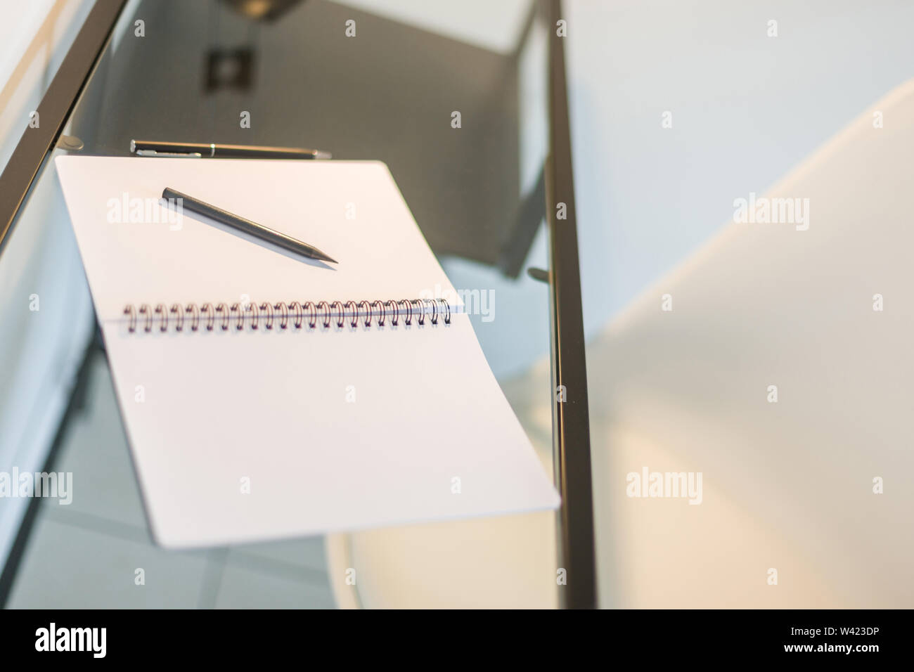 Tilted view of a notebook, pencil and a pen kept on a glass table with ...