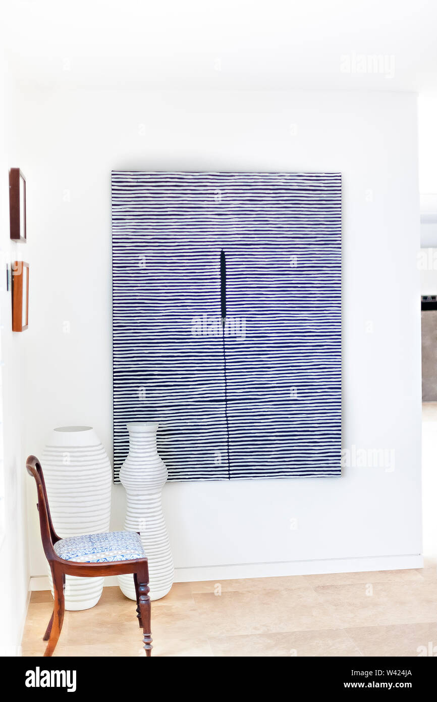 Fancy room with a wooden chair and vases and a pattern art hanging on ...