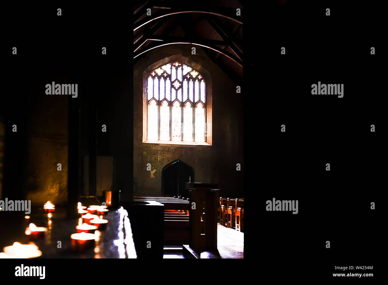 Low light in a dark room with sunlight from a window and small candles ...