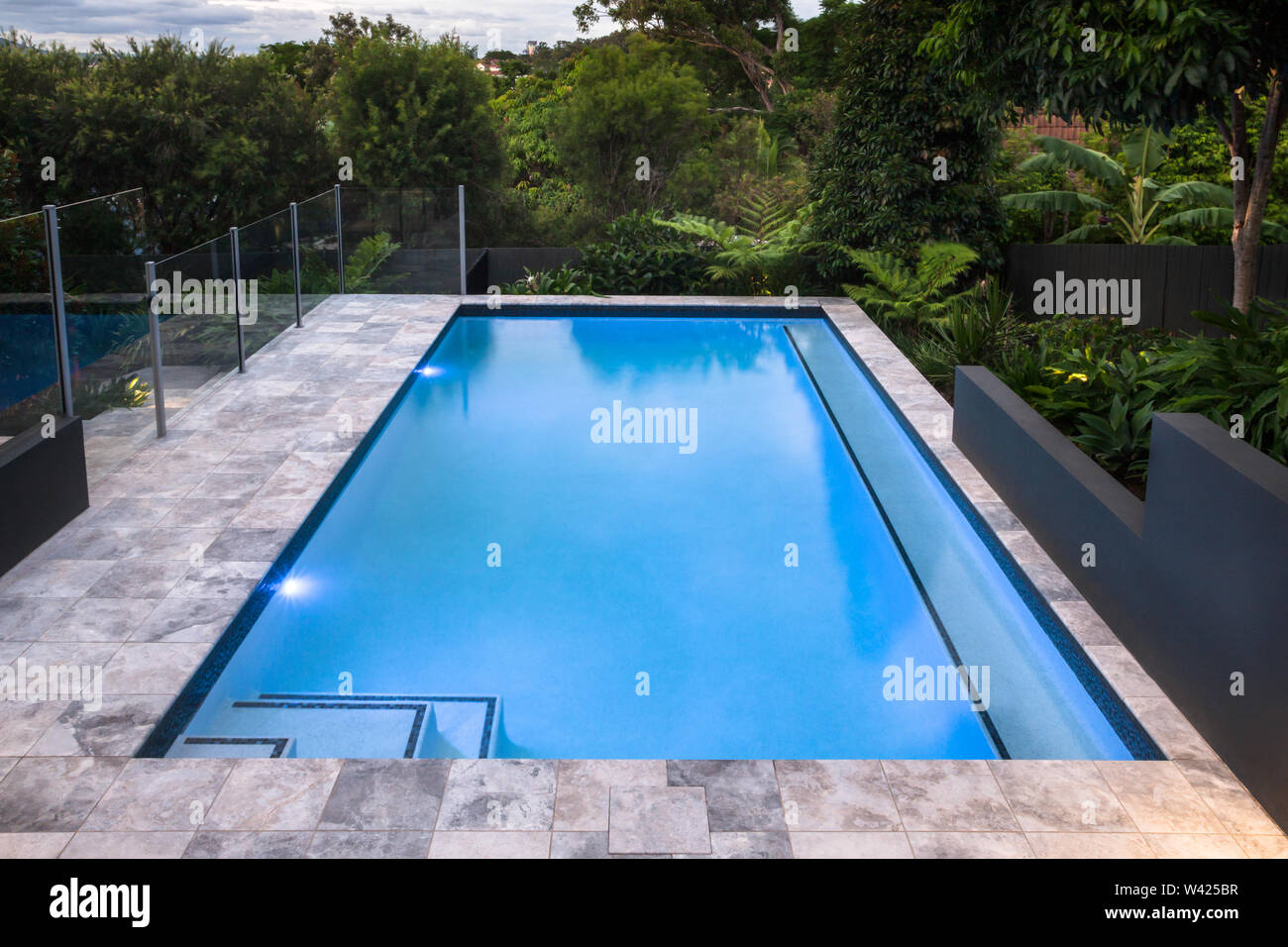 Luxury swimming pool closeup with blue water next to green forest ...