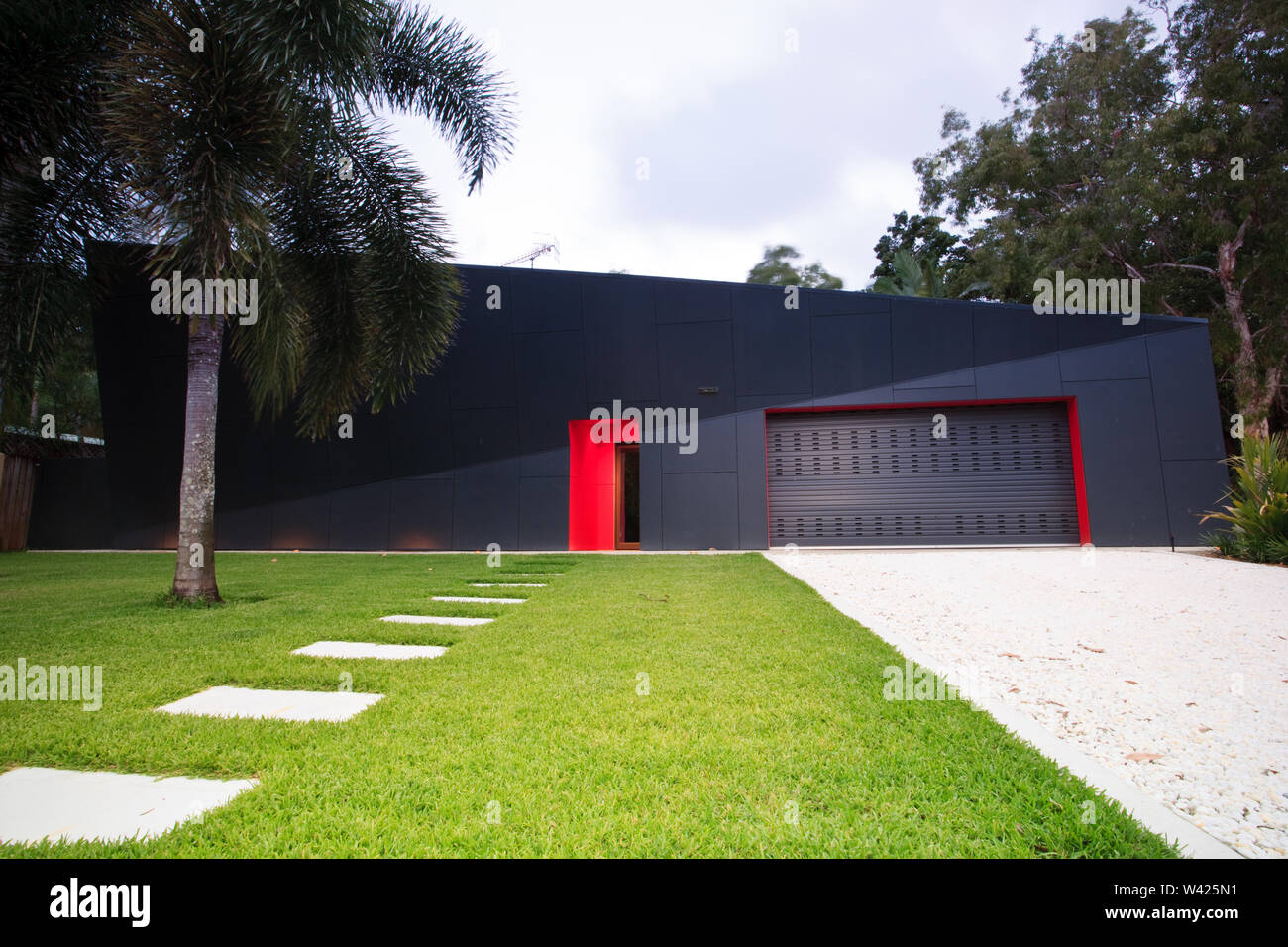 An artsy building exterior with an entrance, a palm tree and grass on ...