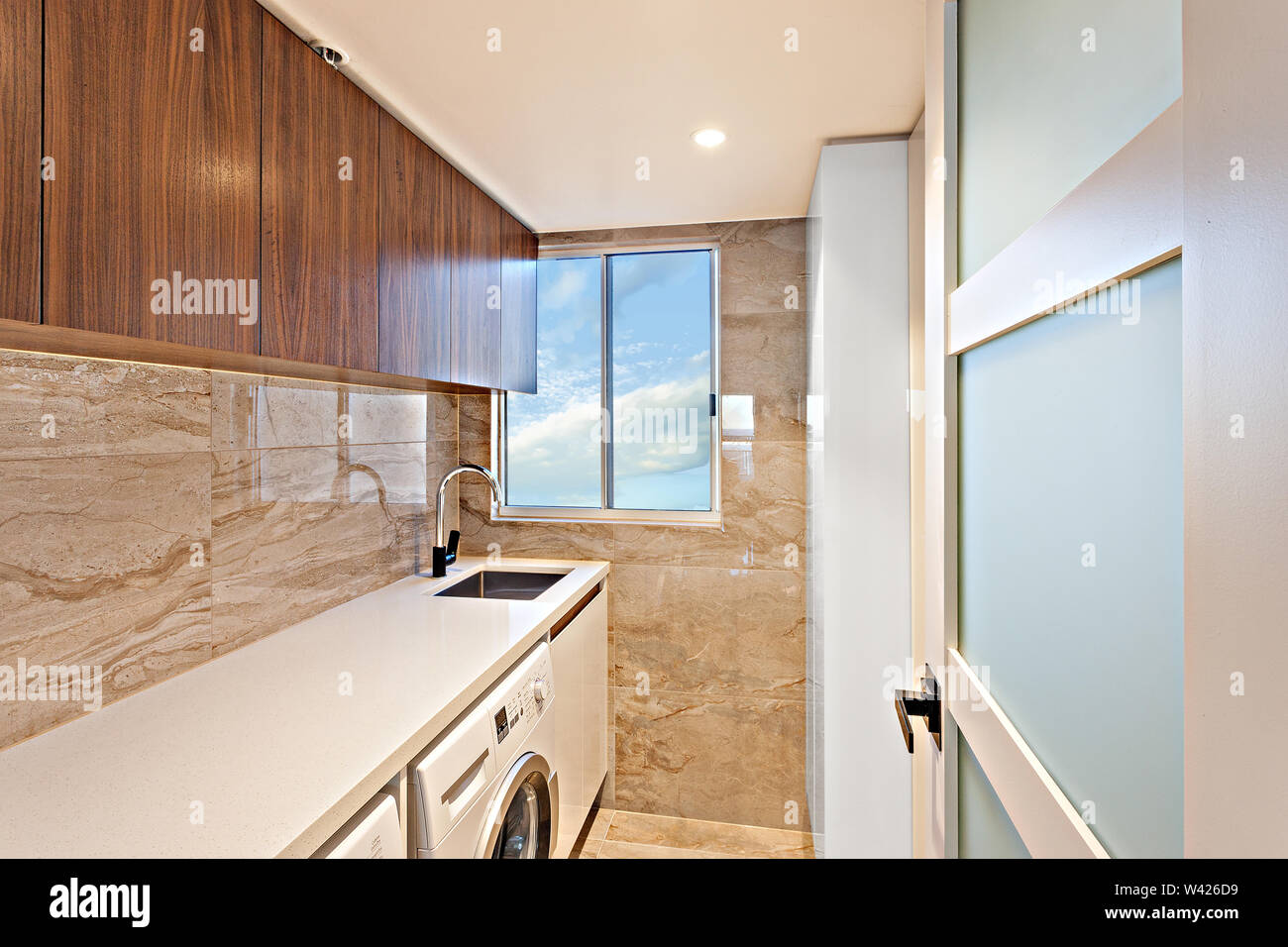 A clean laundry area with cabinets, a basin, and a front-load washing ...