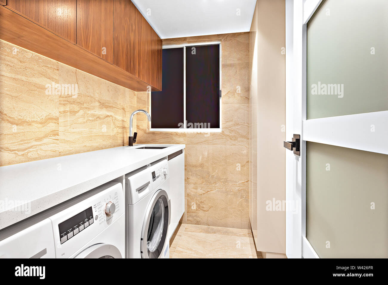 A compact laundry area with tiled floor and walls, two front-load ...