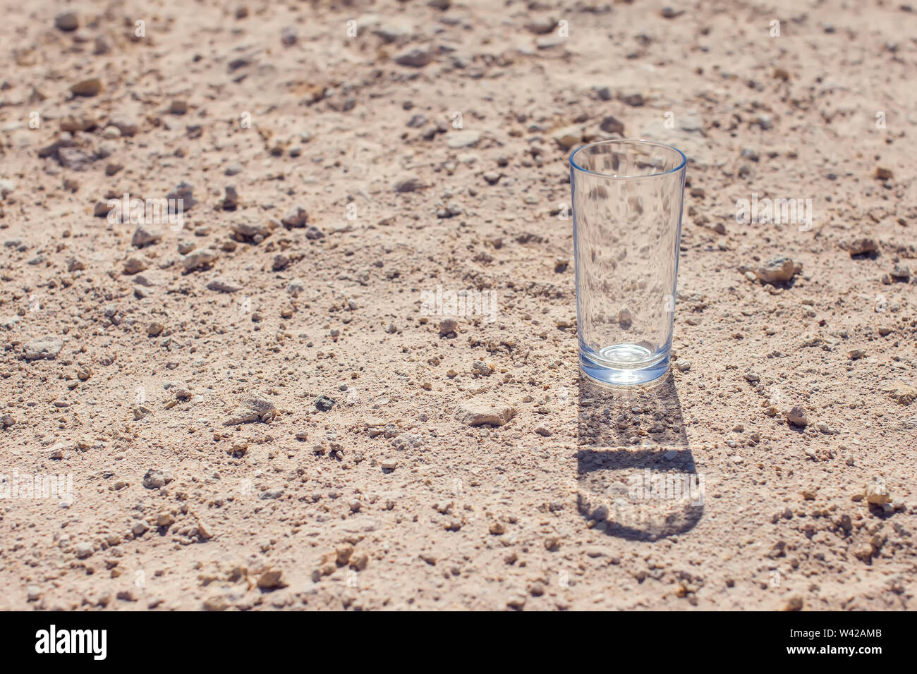 Glass with water on sand in the desert. Thirsty, heat and drought ...
