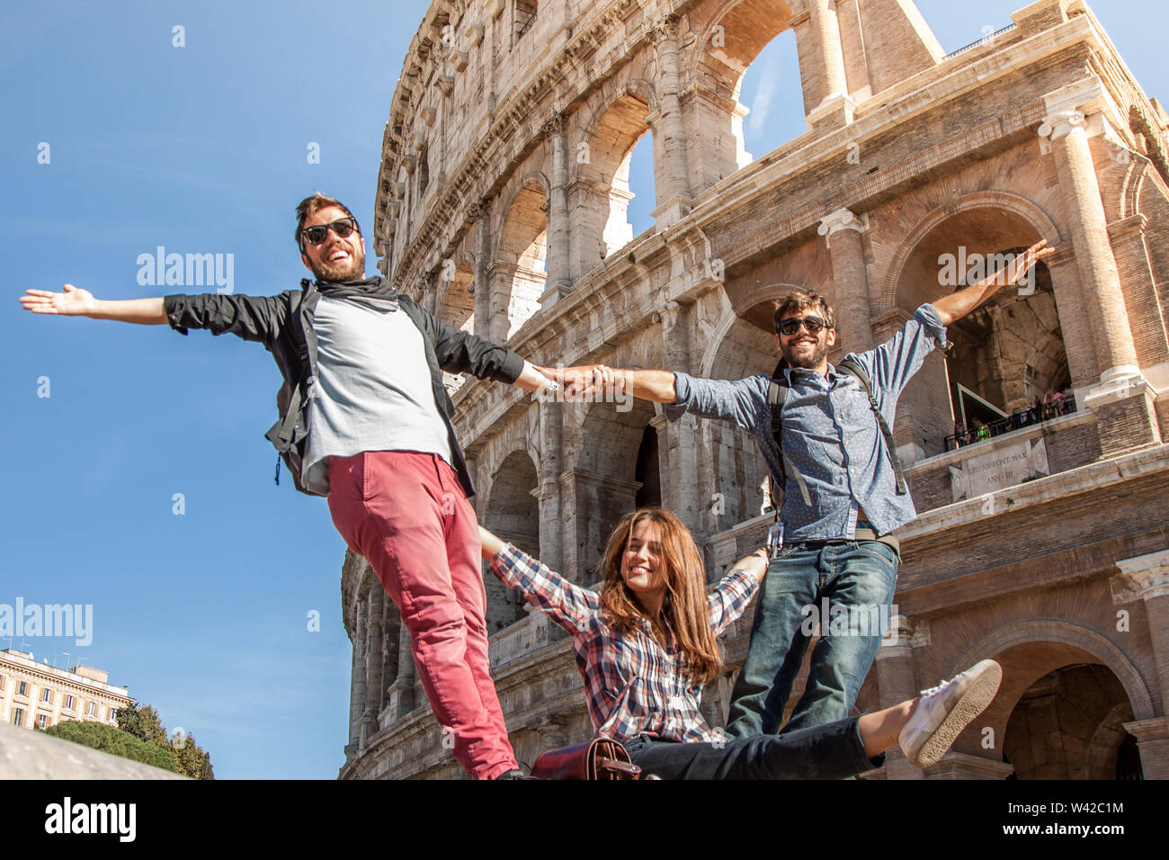 Three happy young friends tourists standing in front of colosseum in ...