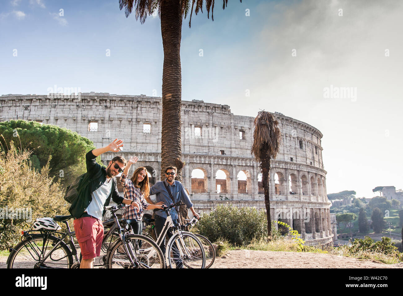 Three happy young friends tourists with bikes at Colosseum in Rome ...