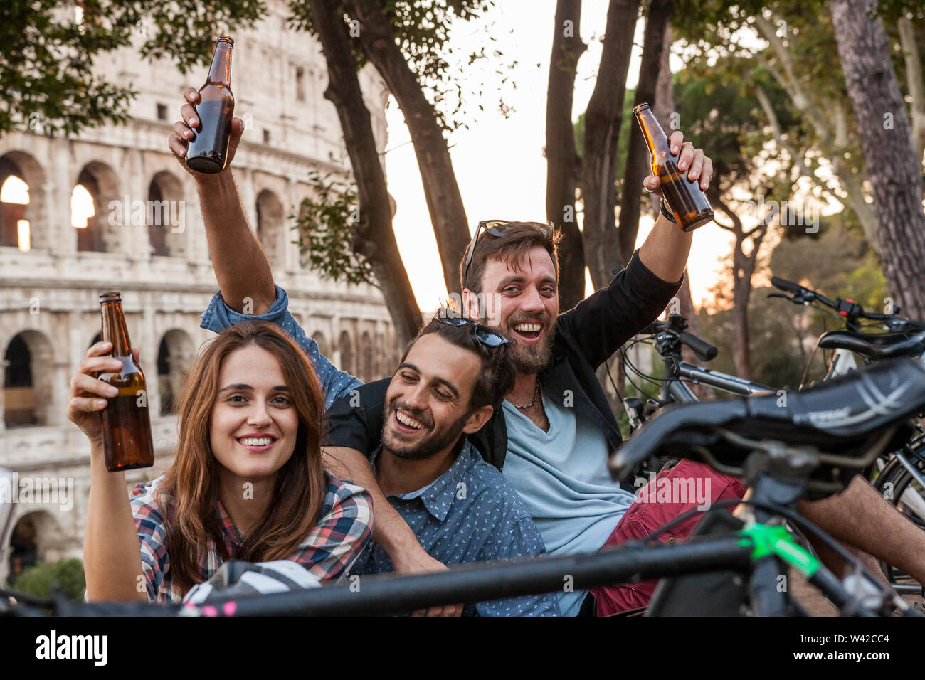 Three happy young friends tourists on a bench at Colosseum in Rome ...