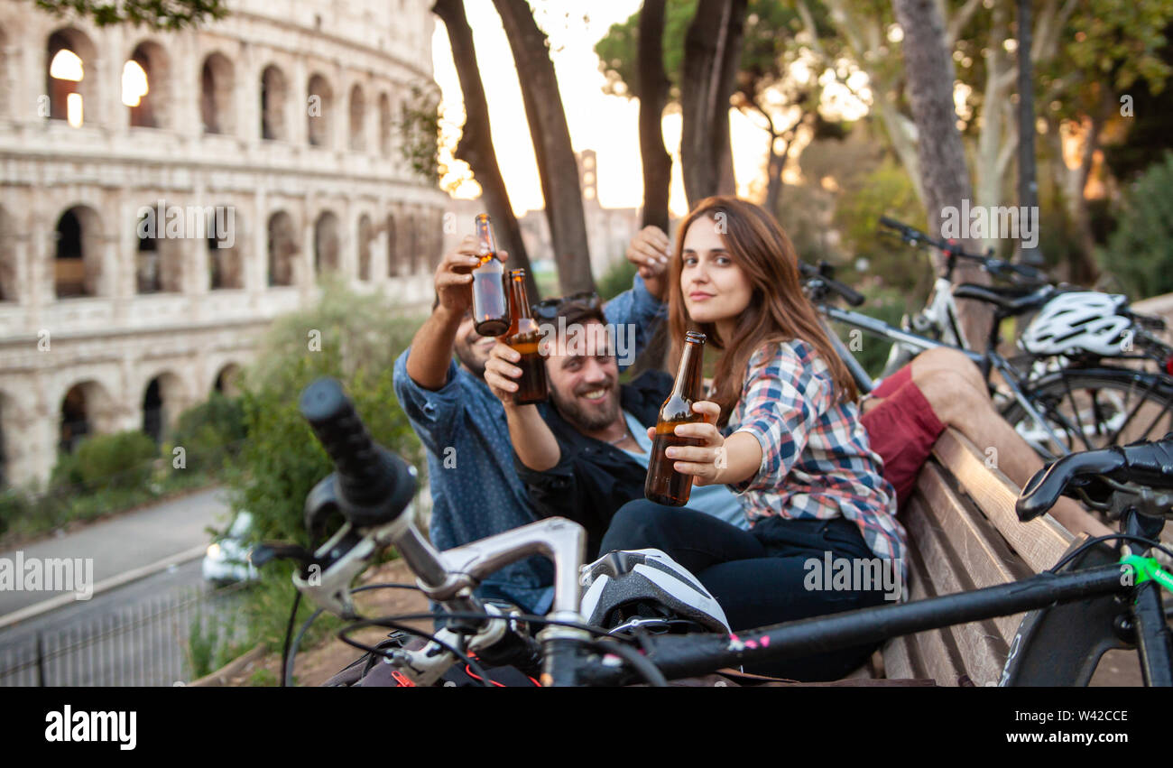 Three happy young friends tourists on a bench at Colosseum in Rome ...