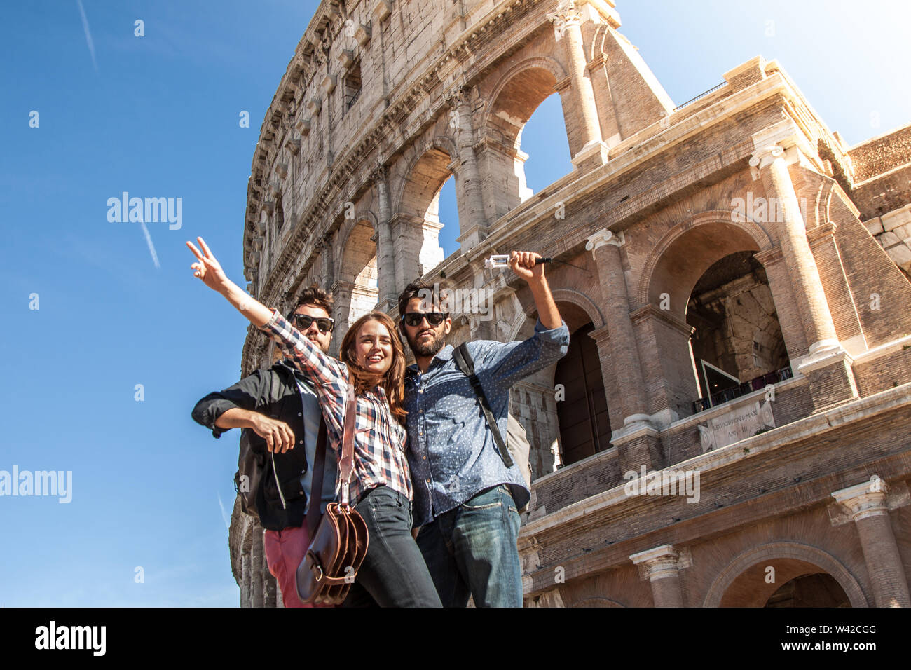 Three happy young friends tourists standing in front of coliseumin rome ...