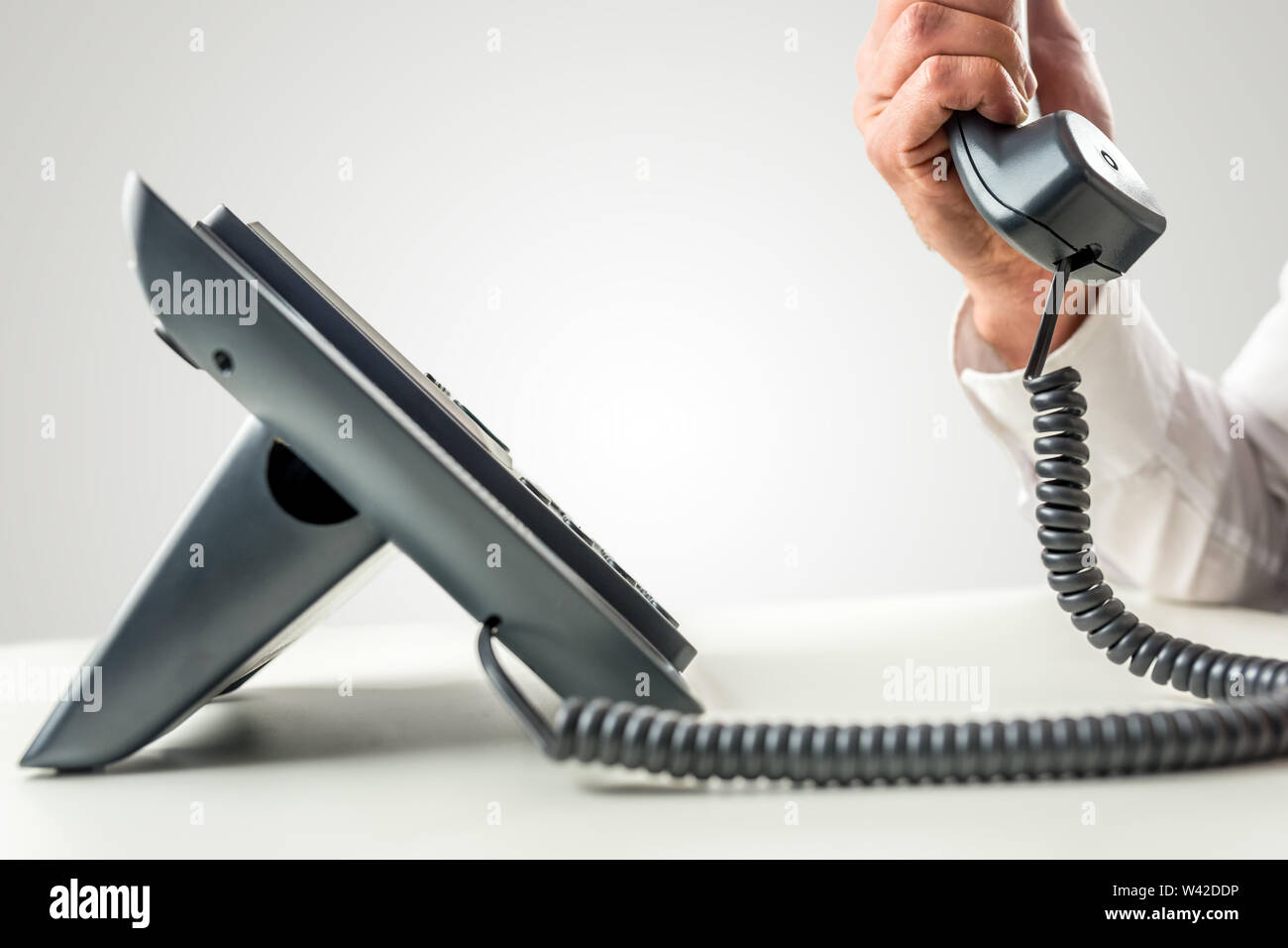 Side view of a black business landline telephone with the receiver held ...