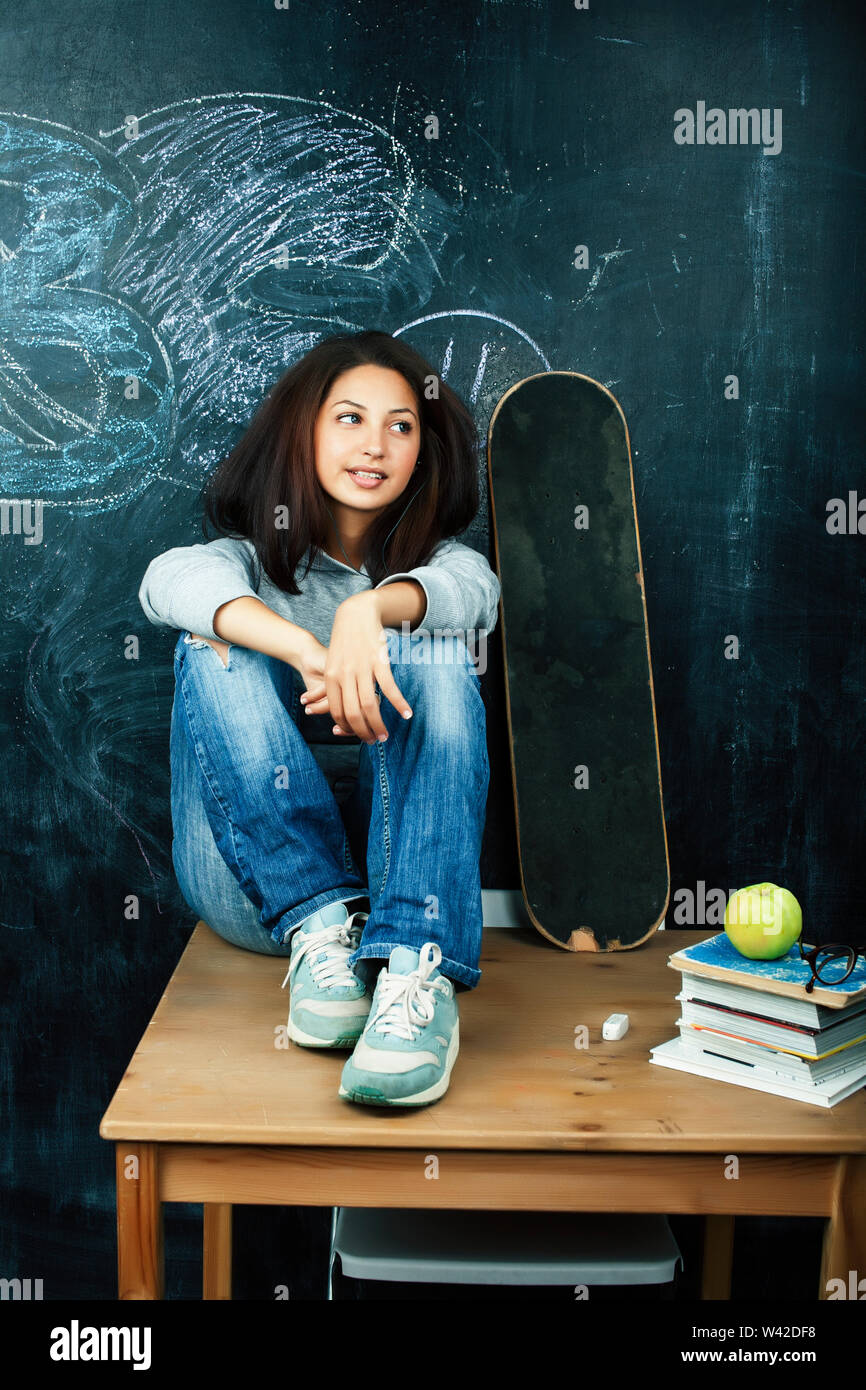 young cute teenage girl in classroom at blackboard seating on table ...