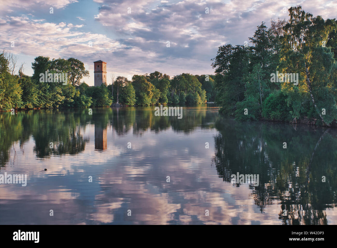 River with reflections from clouds and a tower and forest on the left ...