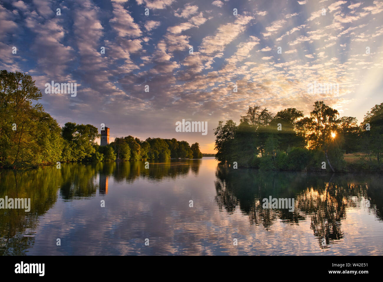 River with reflections from clouds and a tower and forest on the left ...