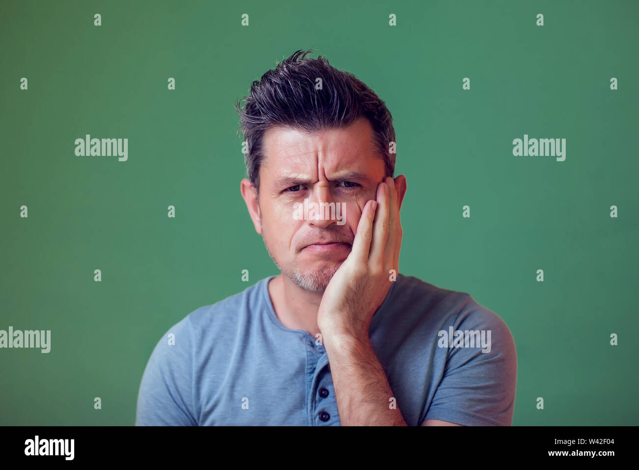 Portrait of frowing young man in casual clothes holding palm on his ...