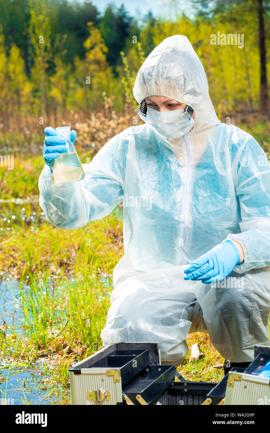 Ecologist with tools and flasks taking water samples from a forest lake ...