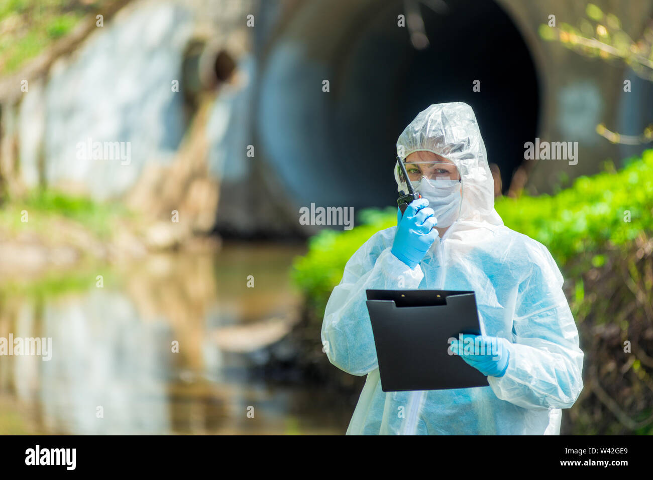 horizontal portrait of a scientist next to a sewer pipe with a walkie ...