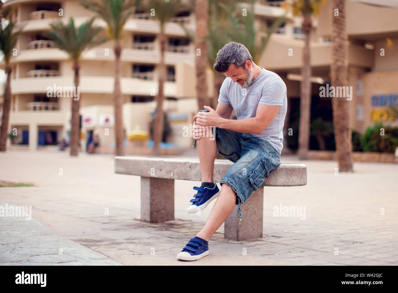Man suffering from knee pain sitting on bench outdoor. People, health ...