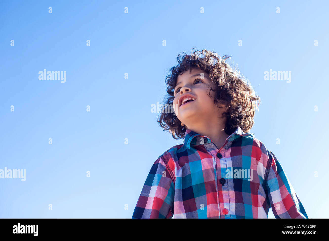 Smiling boy looks up portrait on blue sky background Stock Photo - Alamy