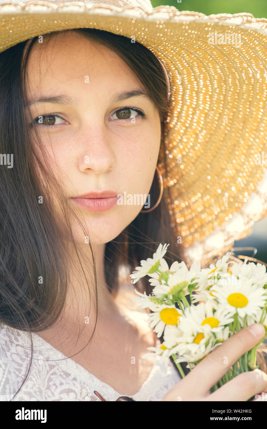 pretty girl in sun hat with camomile bouquet looking at camera, toned ...