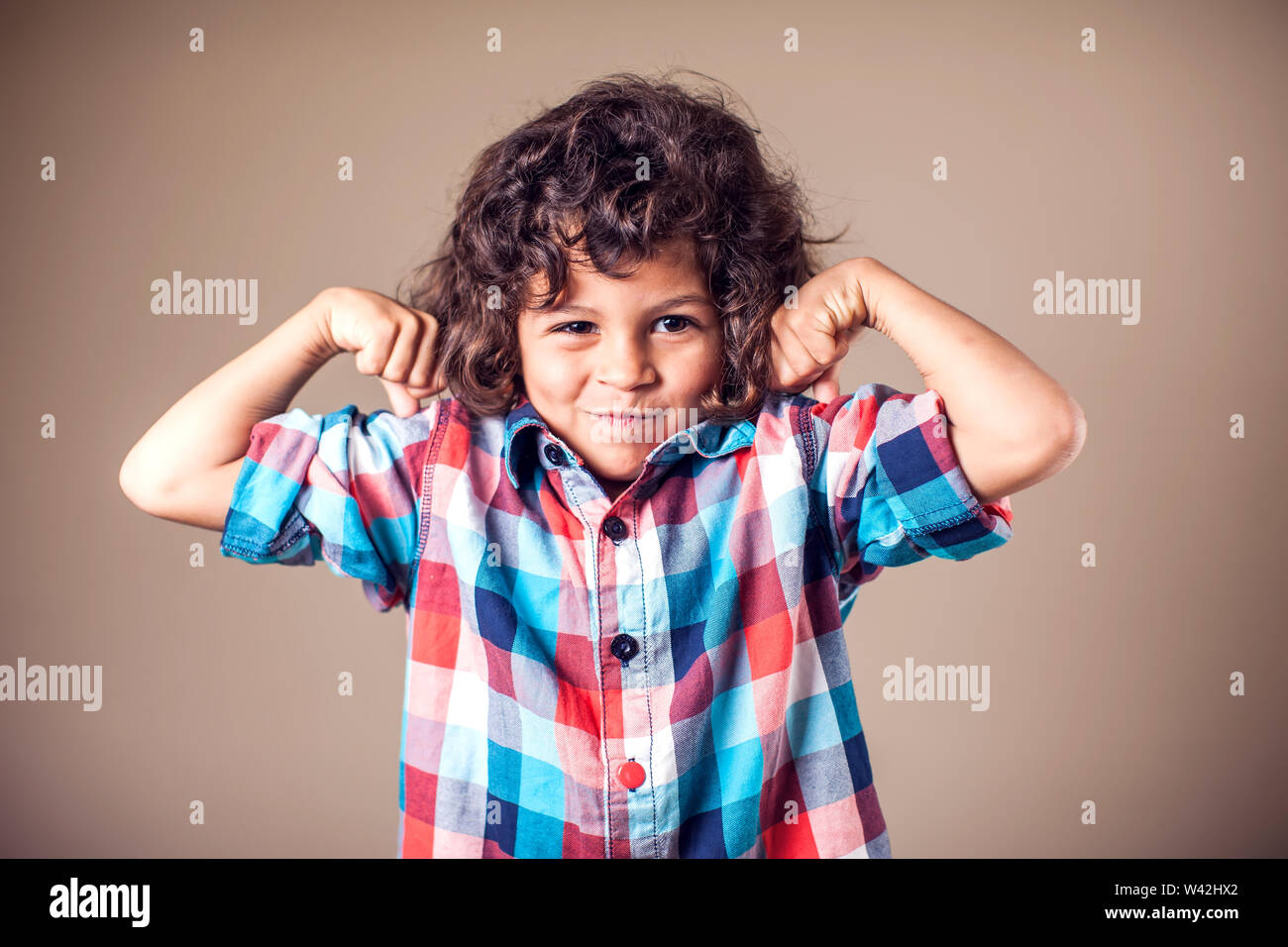 Portrait of a strong kid showing the muscles of his arms on grey ...