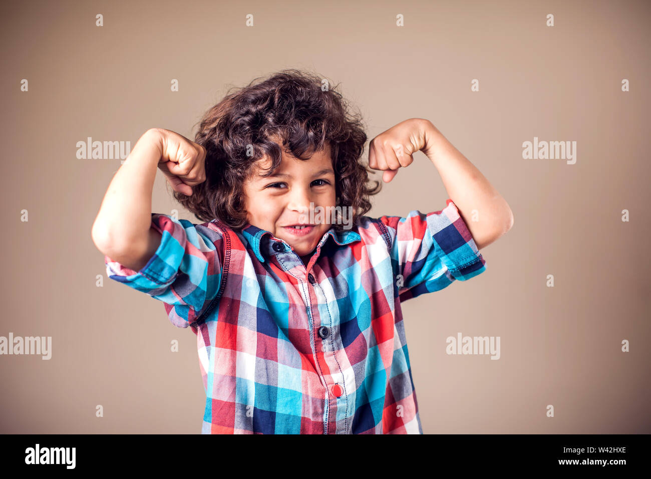 Portrait of a strong kid showing the muscles of his arms on grey ...