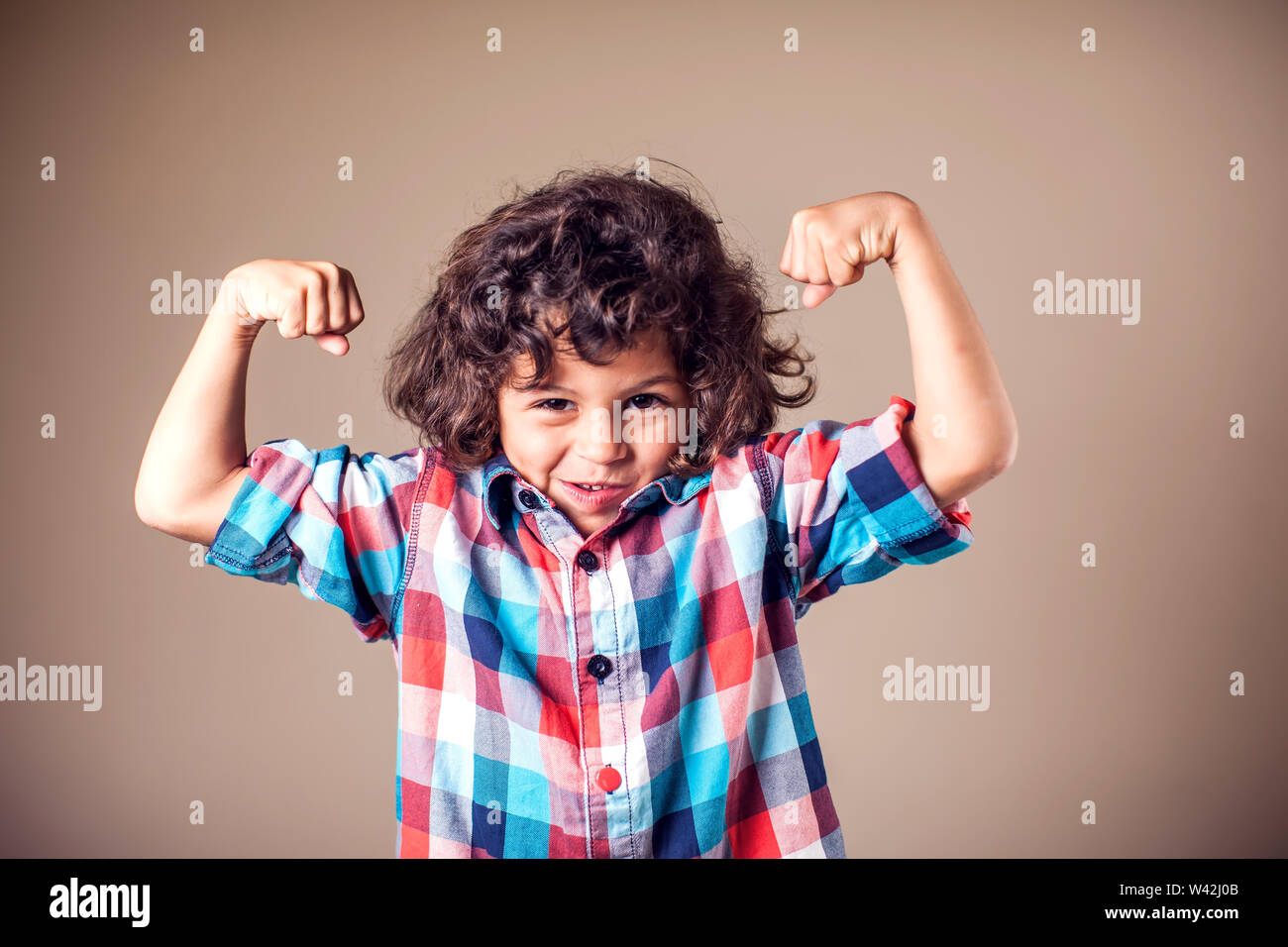 Portrait of a strong kid showing the muscles of his arms on grey ...