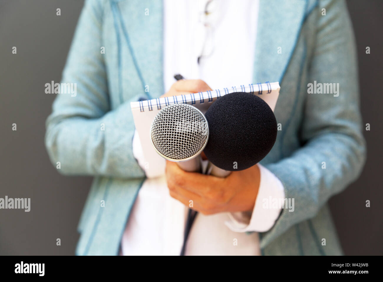 A female journalist standing, holding the microphone and taking notes ...