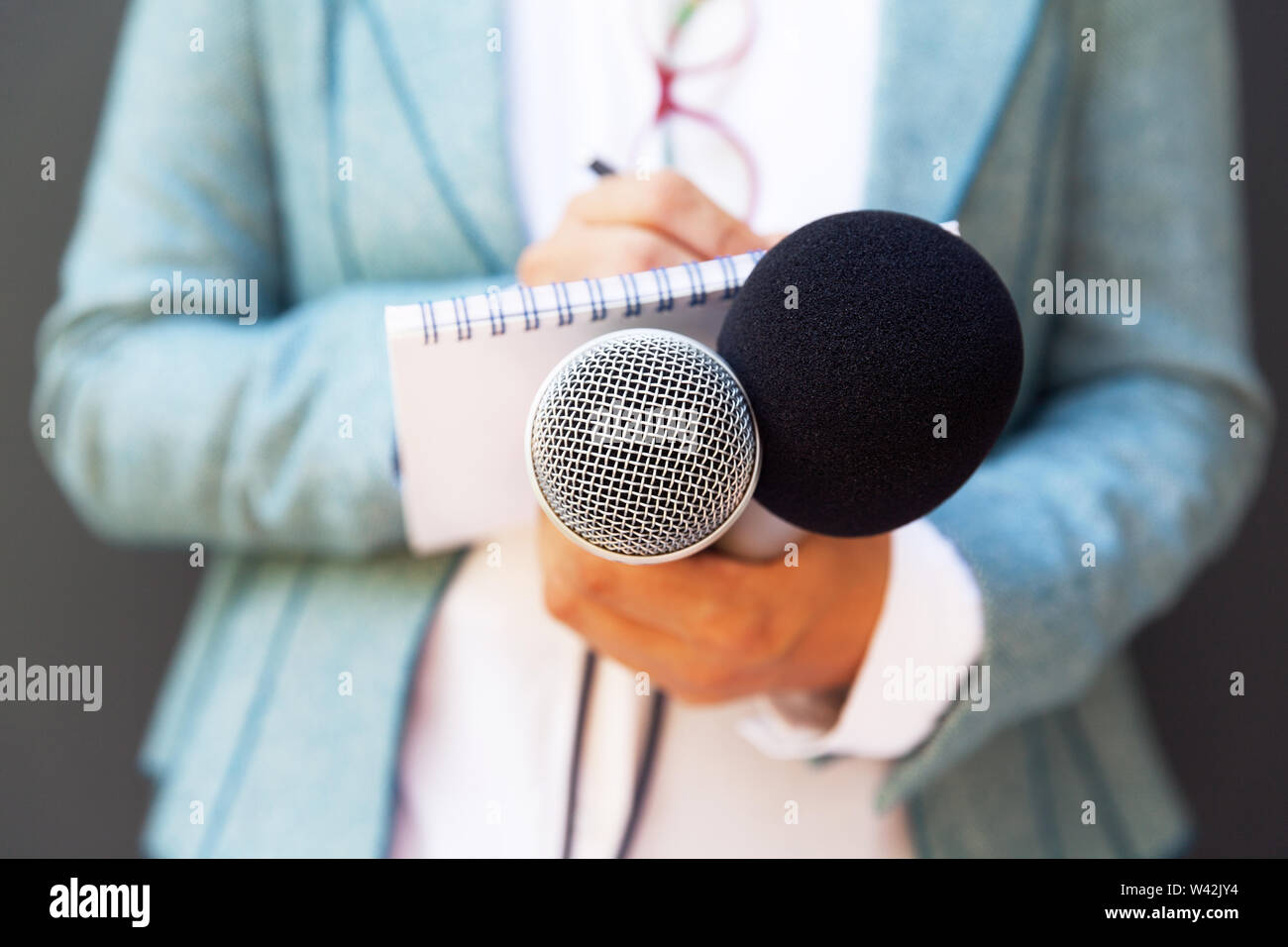 A female journalist standing, holding the microphone and taking notes ...