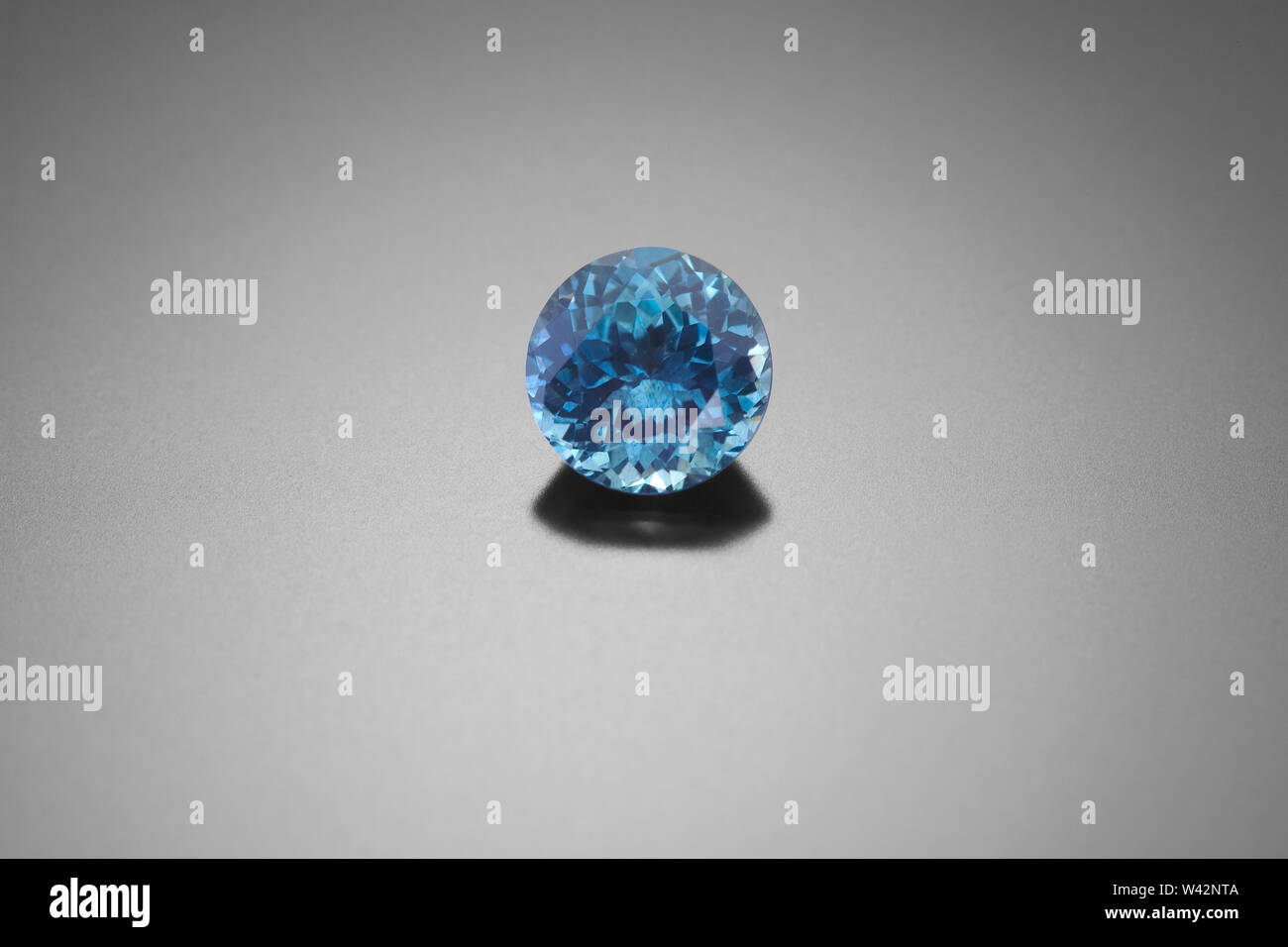 This single round shape faceted sapphire is shown on a grey reflective ...