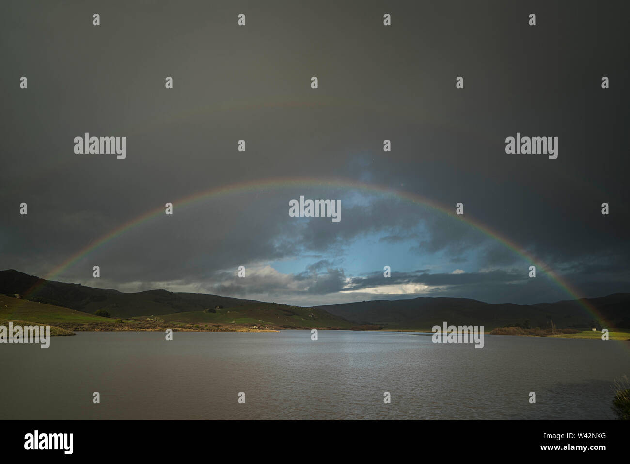 Double rainbow arches across reservoir with storm clouds and hills ...