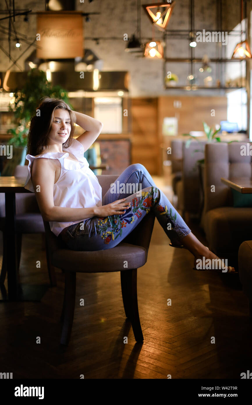 Woman sitting at cafe with feet on back of chair, wearing ethnic jeans ...