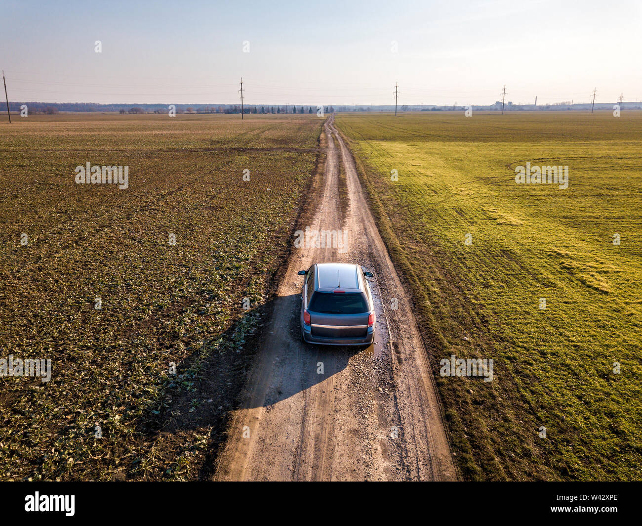 Aerial view of car driving by straight ground road through green fields ...