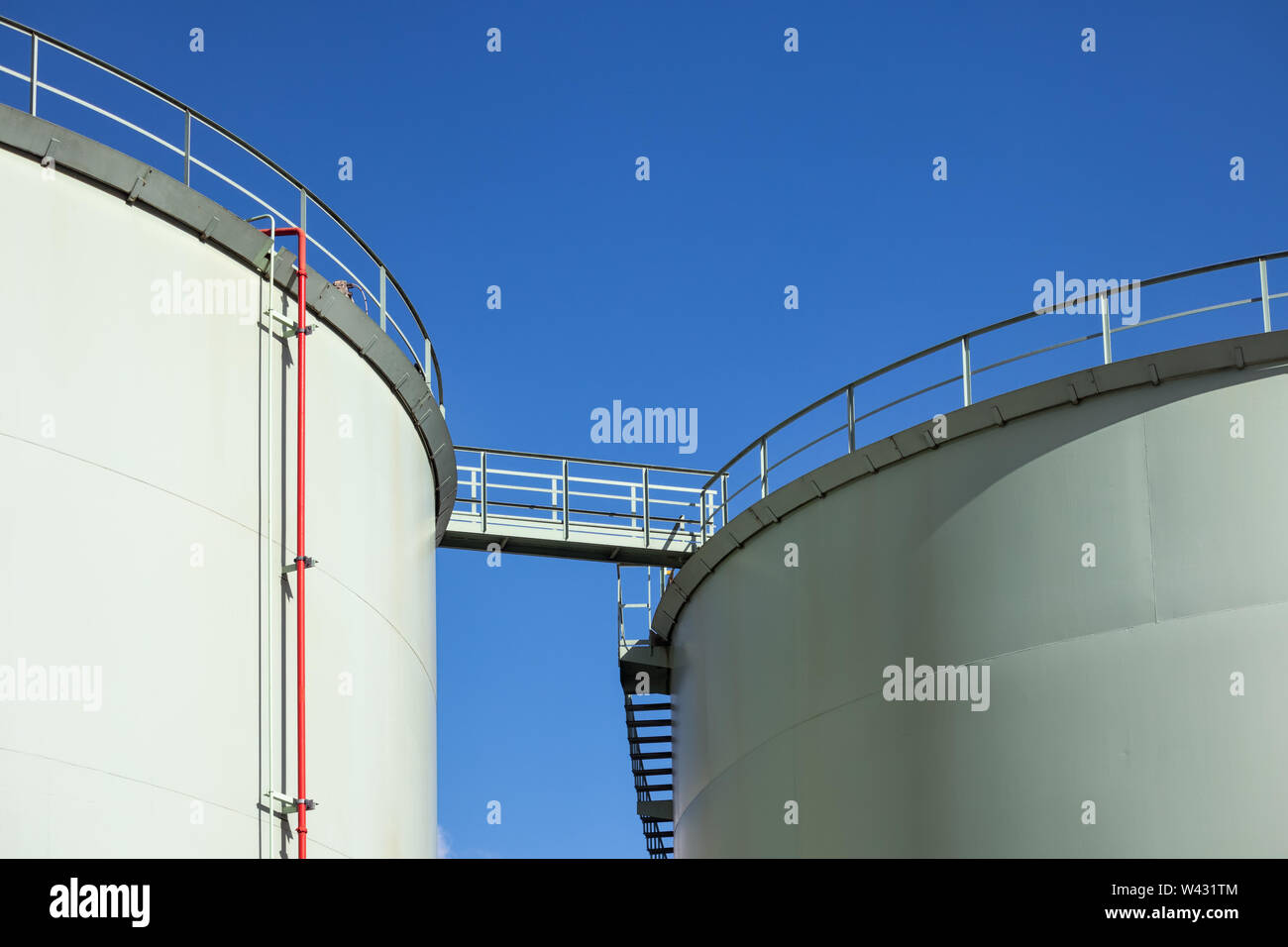 Fuel storage tanks with catwalk bridge against blue sky Stock Photo - Alamy