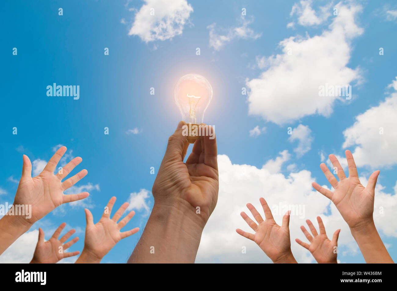 glowing light bulb in hand and many hands reaching for this light bulb ...