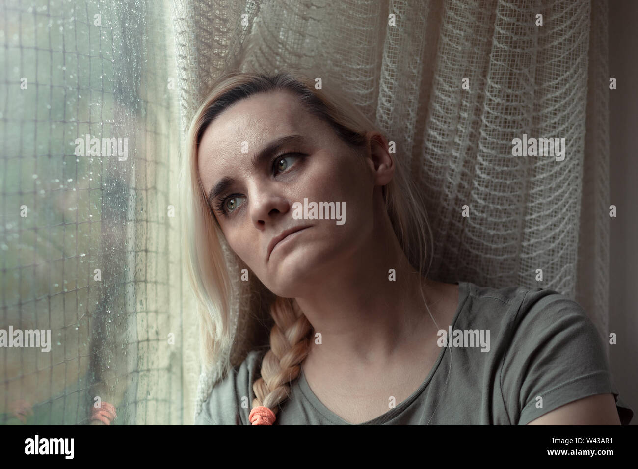 Sad, depressed woman sitting by the window, looking longingly out and ...