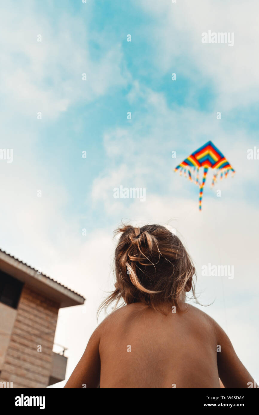 Happy child launches a kite, baby looking up at a multi-colored kite ...