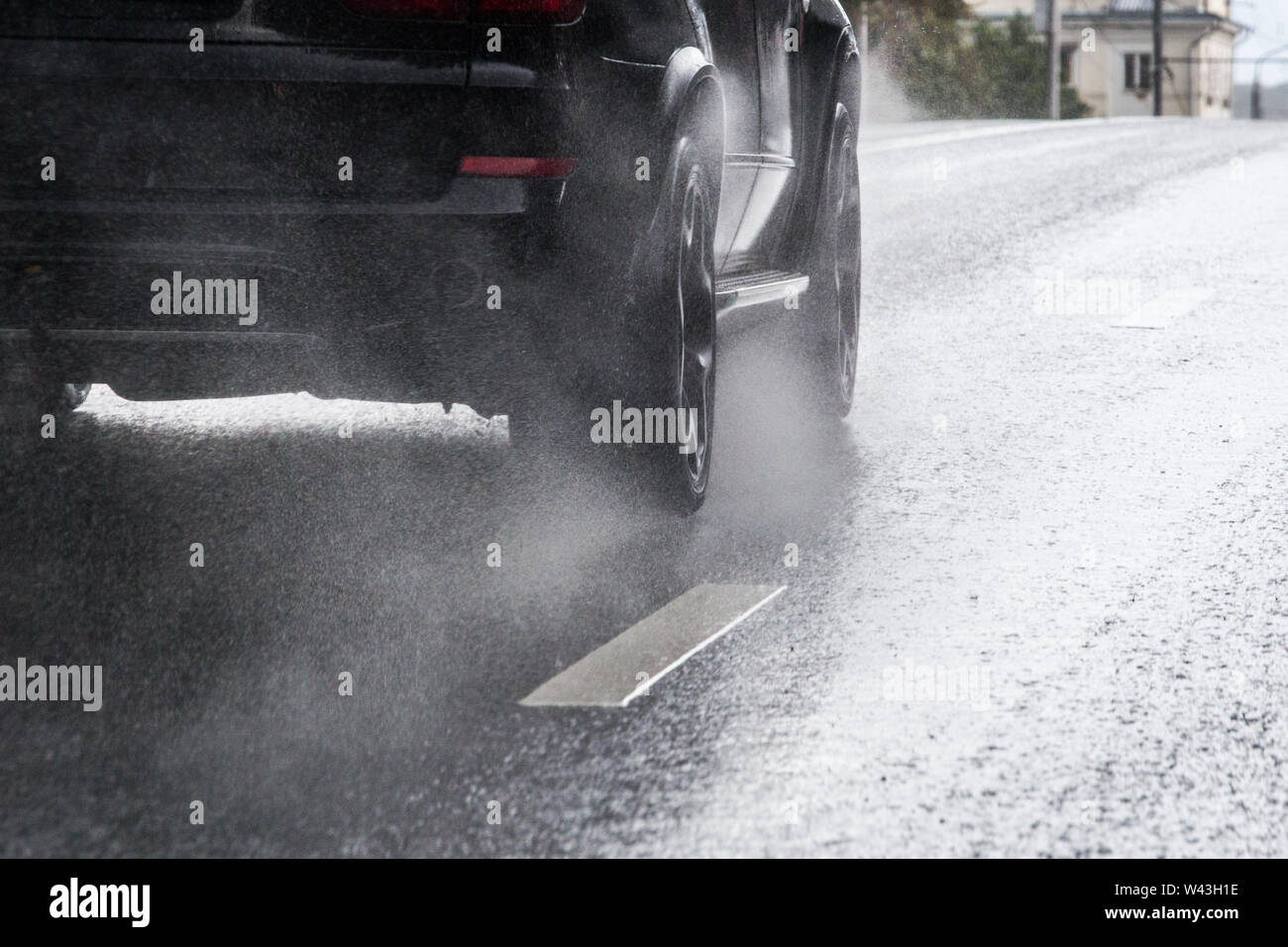 Rain water splash flow from wheels of black car moving fast in daylight ...