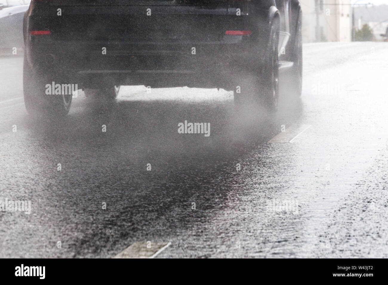 Rain water splash flow from wheels of black car moving fast in daylight ...