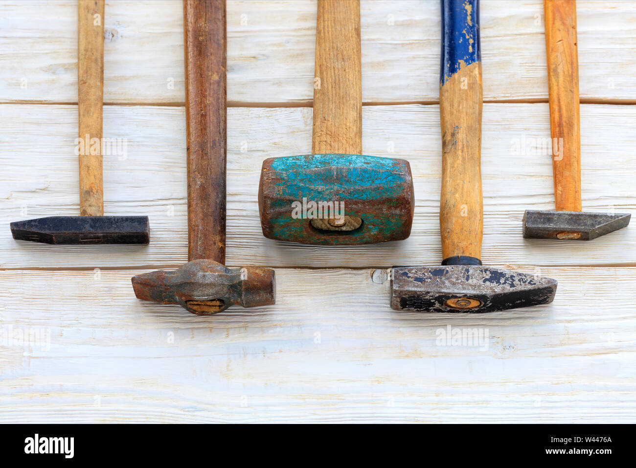 Old worn iron hammers with wooden handles lie on a white wooden table ...